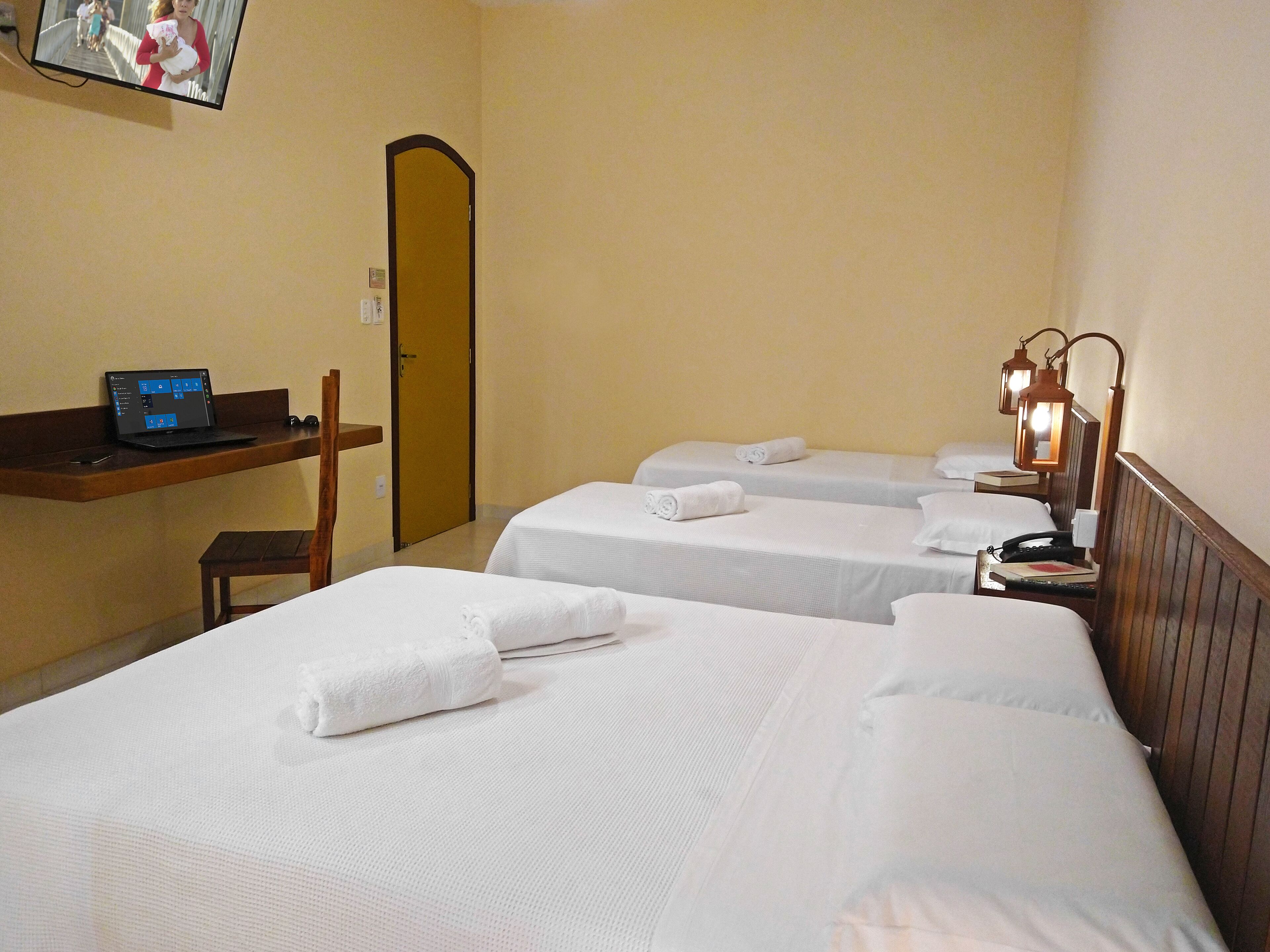 Quarto de hotel com duas camas, um laptop numa prateleira e uma porta.