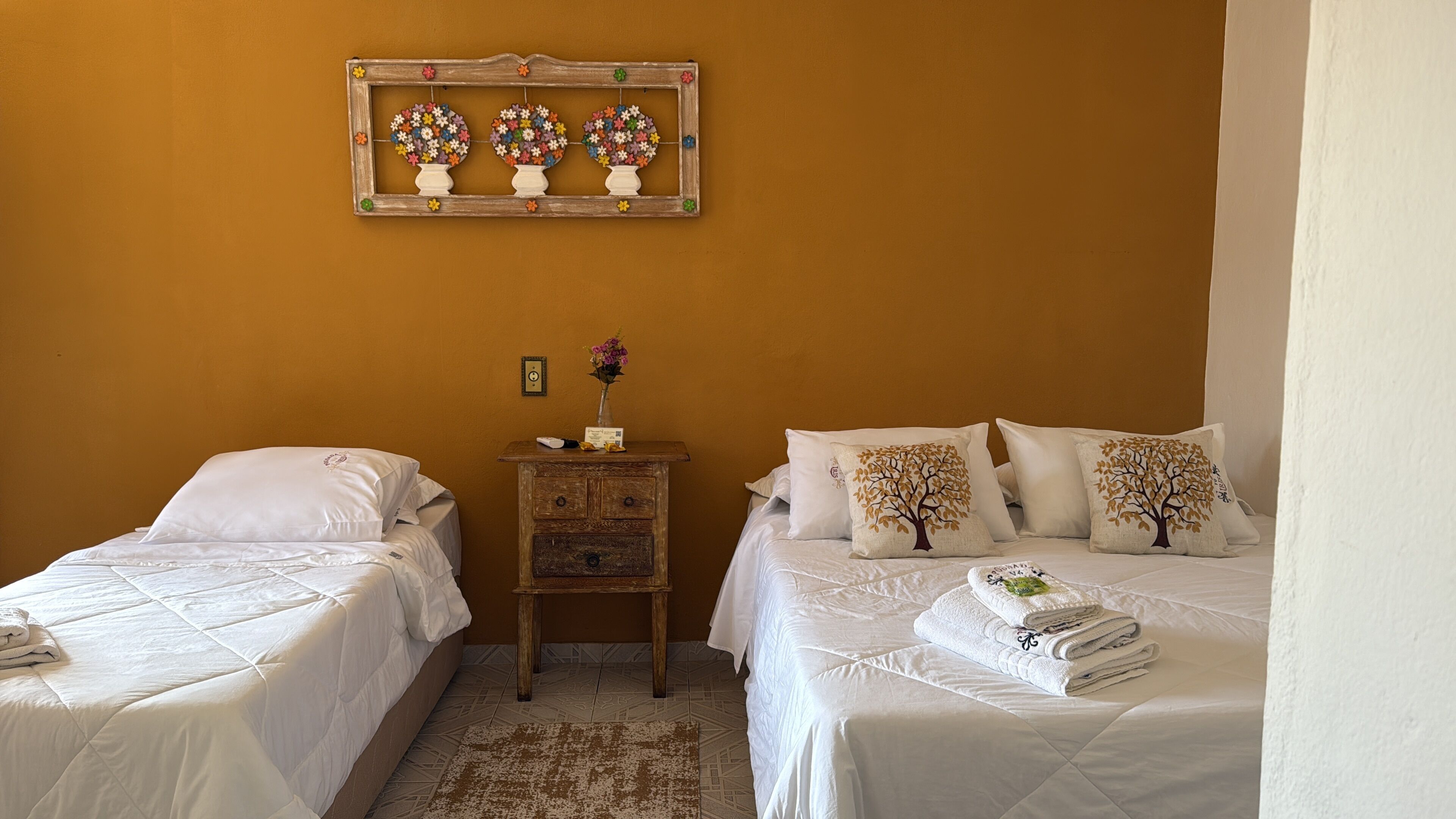 Quarto de hotel com duas camas, uma mesa de cabeceira de madeira e um objeto decorativo na parede.