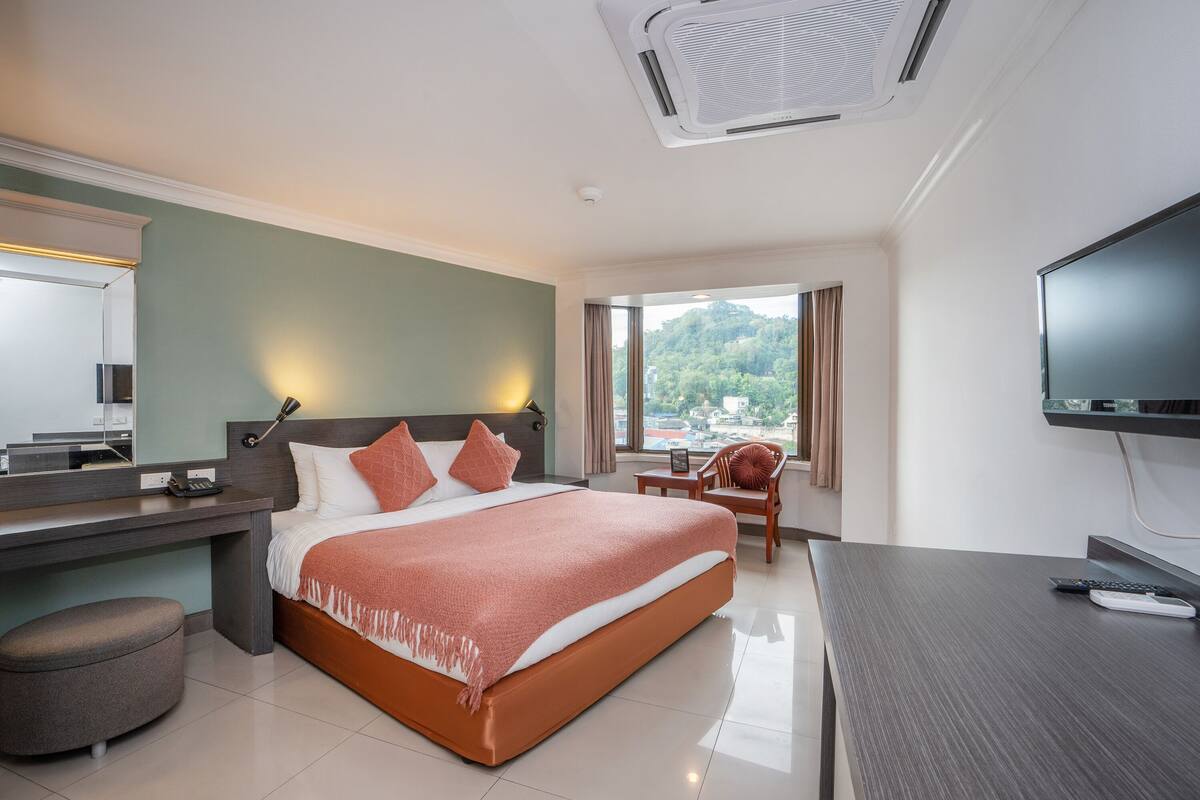 Quarto de hotel moderno com uma cama grande, uma escrivaninha, uma cadeira e uma televisão.