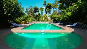 Piscina retangular com deck ao redor, bancos e grade.