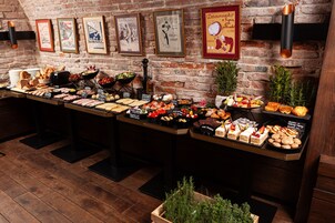 Buffet com diversos alimentos e parede de tijolos com quadros.