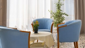 Um quarto com uma mesa redonda, duas poltronas azuis, um vaso de planta e um candelabro.