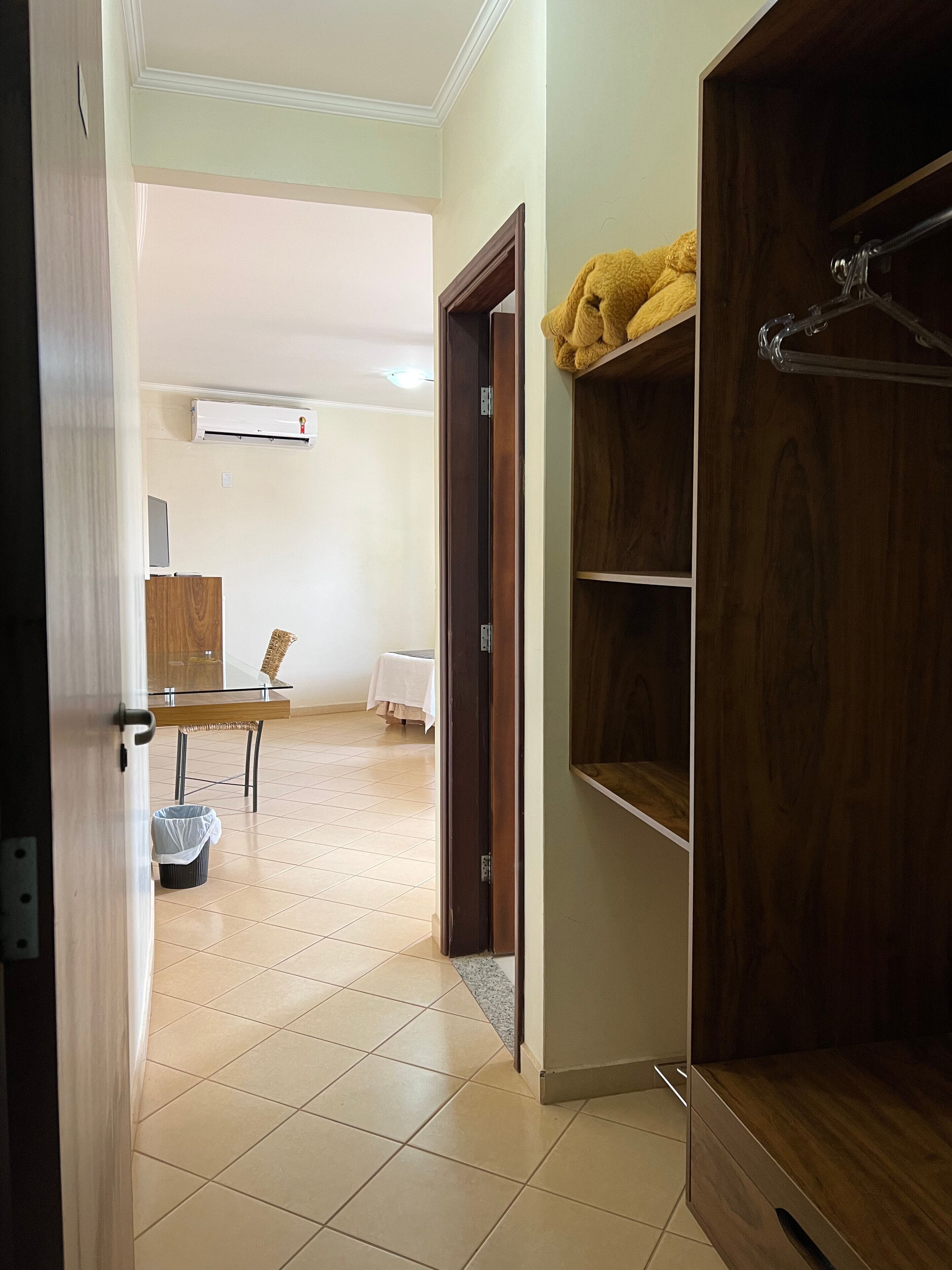 Quarto com guarda-roupa de madeira, chão em azulejos e uma pequena mesa com uma cadeira.