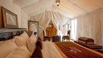 Um quarto com tenda, uma cama grande, um candelabro e uma mesinha com uma lâmpada.