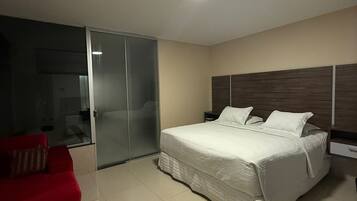 Quarto de hotel com uma cama, um sofá vermelho, um guarda-roupa com porta de vidro e uma cabeceira de madeira.