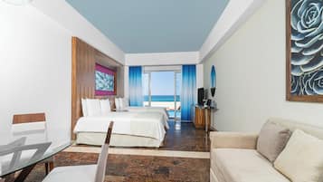 Quarto de hotel com cama, mesa de vidro, sofá e vista para o mar.