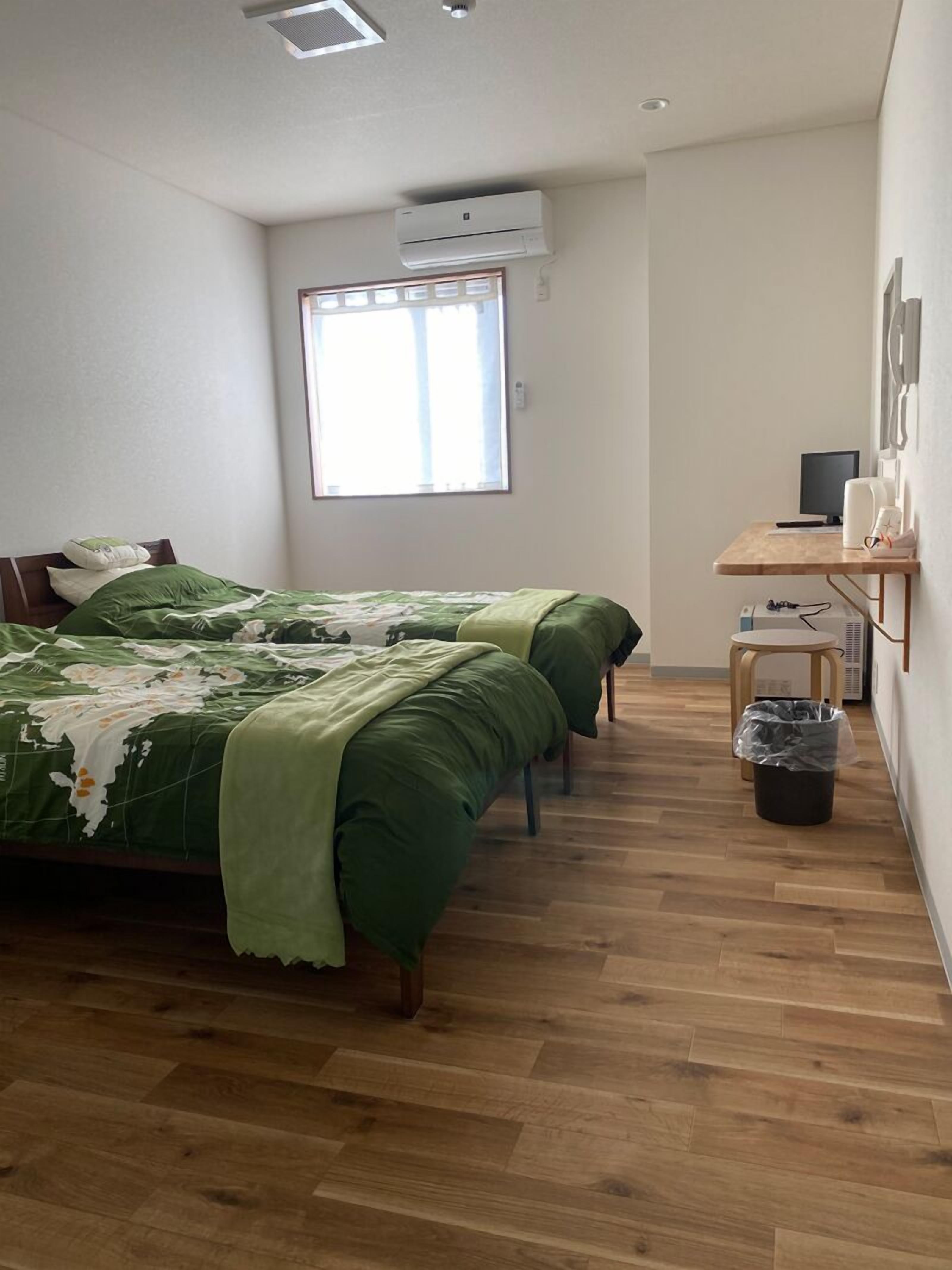 Quarto com duas camas, uma escrivaninha, uma cadeira, um cesto de lixo e um aparelho de ar condicionado.