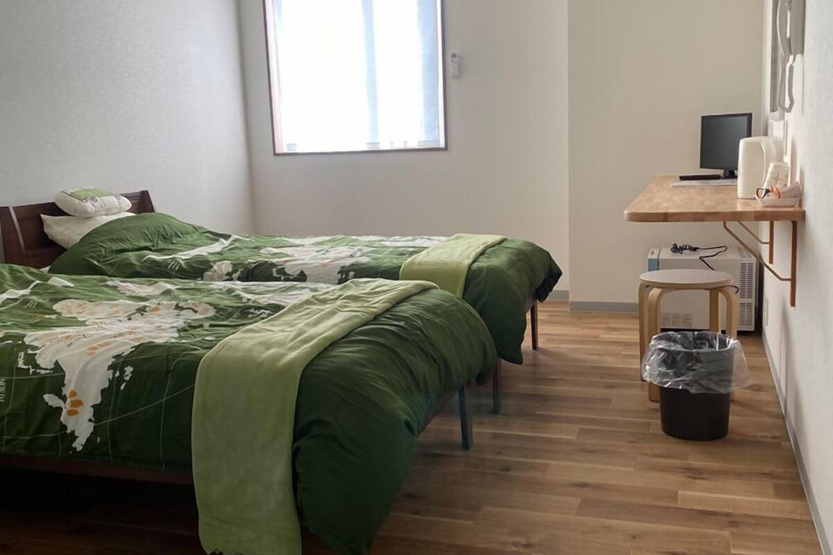 Quarto com duas camas, uma escrivaninha, uma cadeira, um cesto de lixo e um aparelho de ar condicionado.