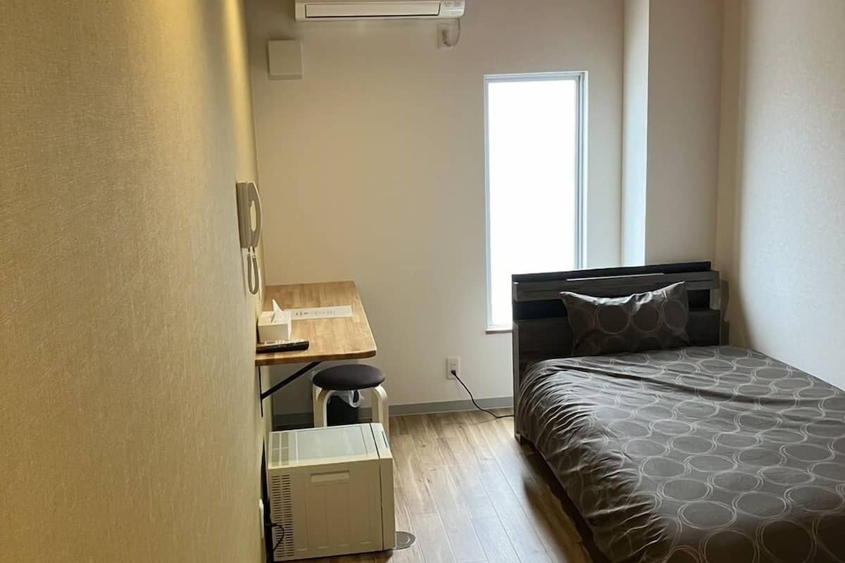 Um quarto com cama, escrivaninha, cadeira e ar condicionado.