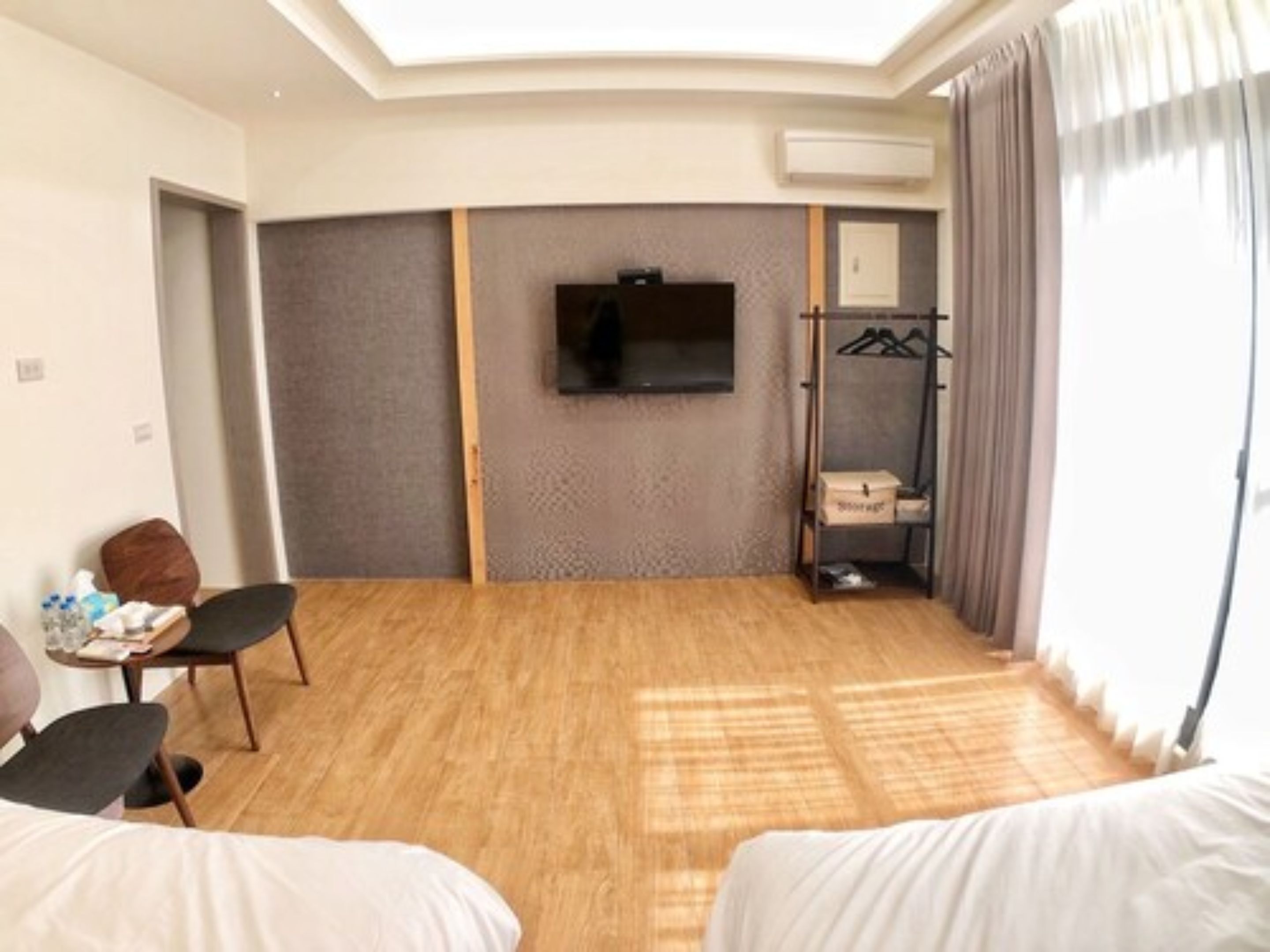 Quarto de hotel com cama, escrivaninha, cadeira, televisão fixada na parede, cabideiro e janela com cortinas.