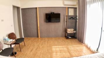 Quarto de hotel com cama, escrivaninha, cadeira, televisão fixada na parede, cabideiro e janela com cortinas.