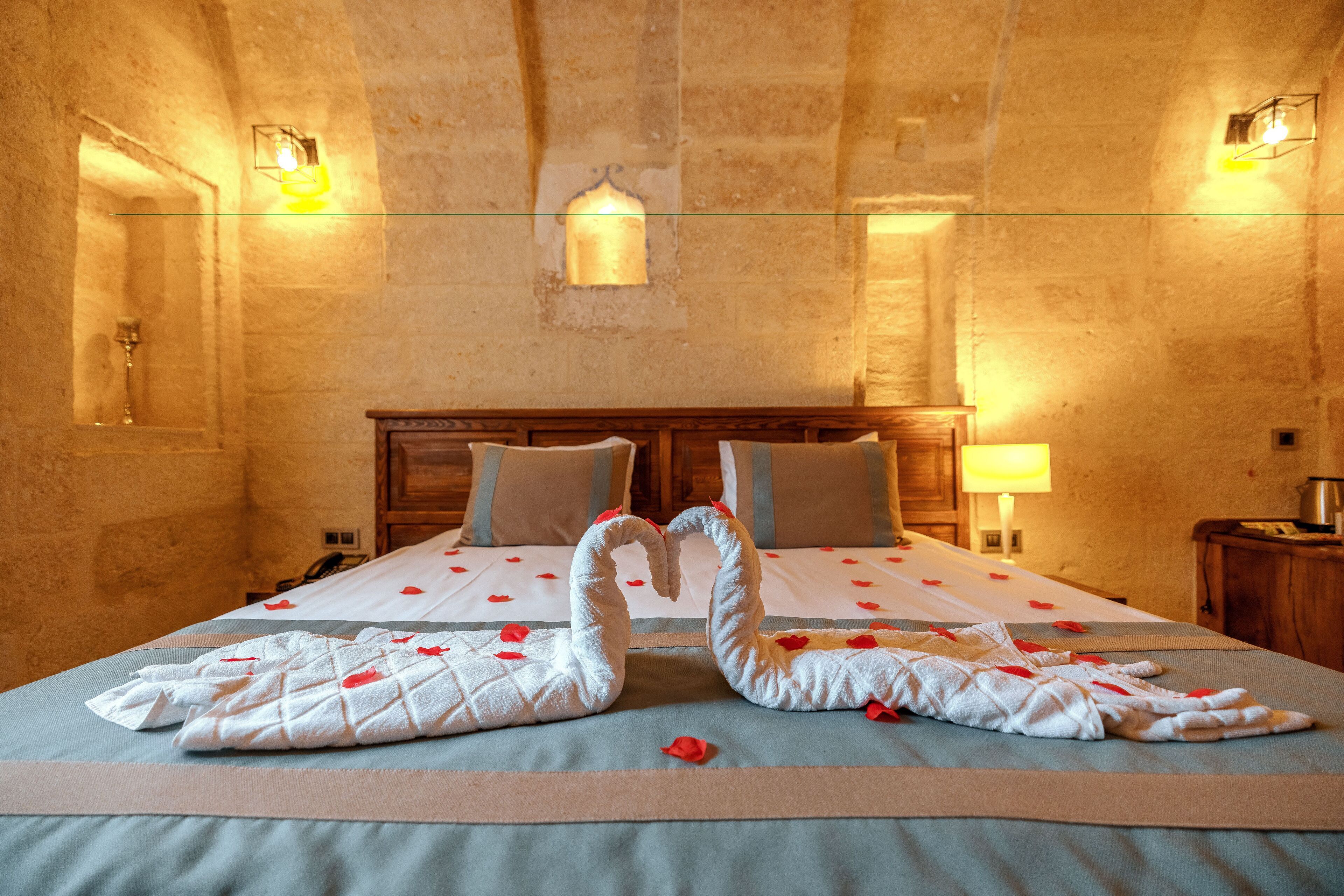 Quarto de hotel com uma cama grande, duas luminárias fixadas na parede e uma cabeceira de madeira.