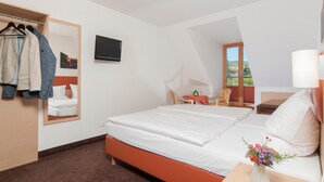 Quarto de hotel com cama, televisão, área de estar com mesa e cadeiras, e janela com vista.