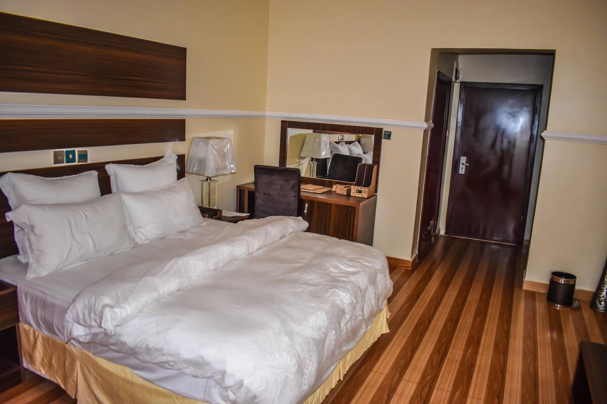Quarto de hotel com uma cama grande, uma escrivaninha com cadeira, um espelho e uma porta.