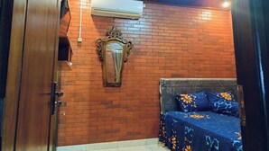 Quarto com parede de tijolos, cama com roupa de cama estampada, aparelho de ar condicionado e espelho decorativo.