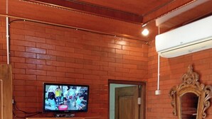 Quarto com parede de tijolos, televisão fixada, porta de madeira e espelho na parede.