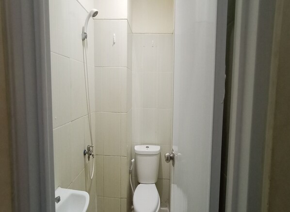 Uma casa de banho pequena com sanita, chuveiro e lavatório.