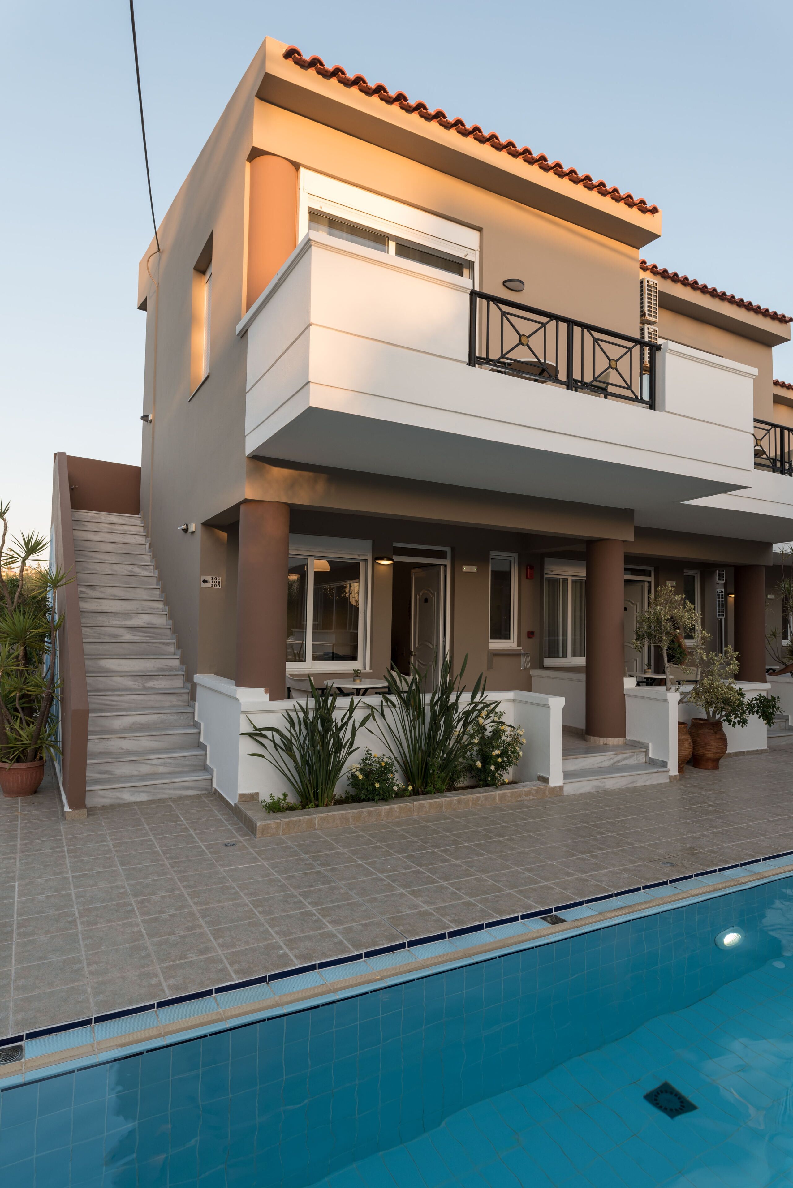 Uma casa moderna de dois andares com piscina, com varanda e escadaria que leva à entrada.