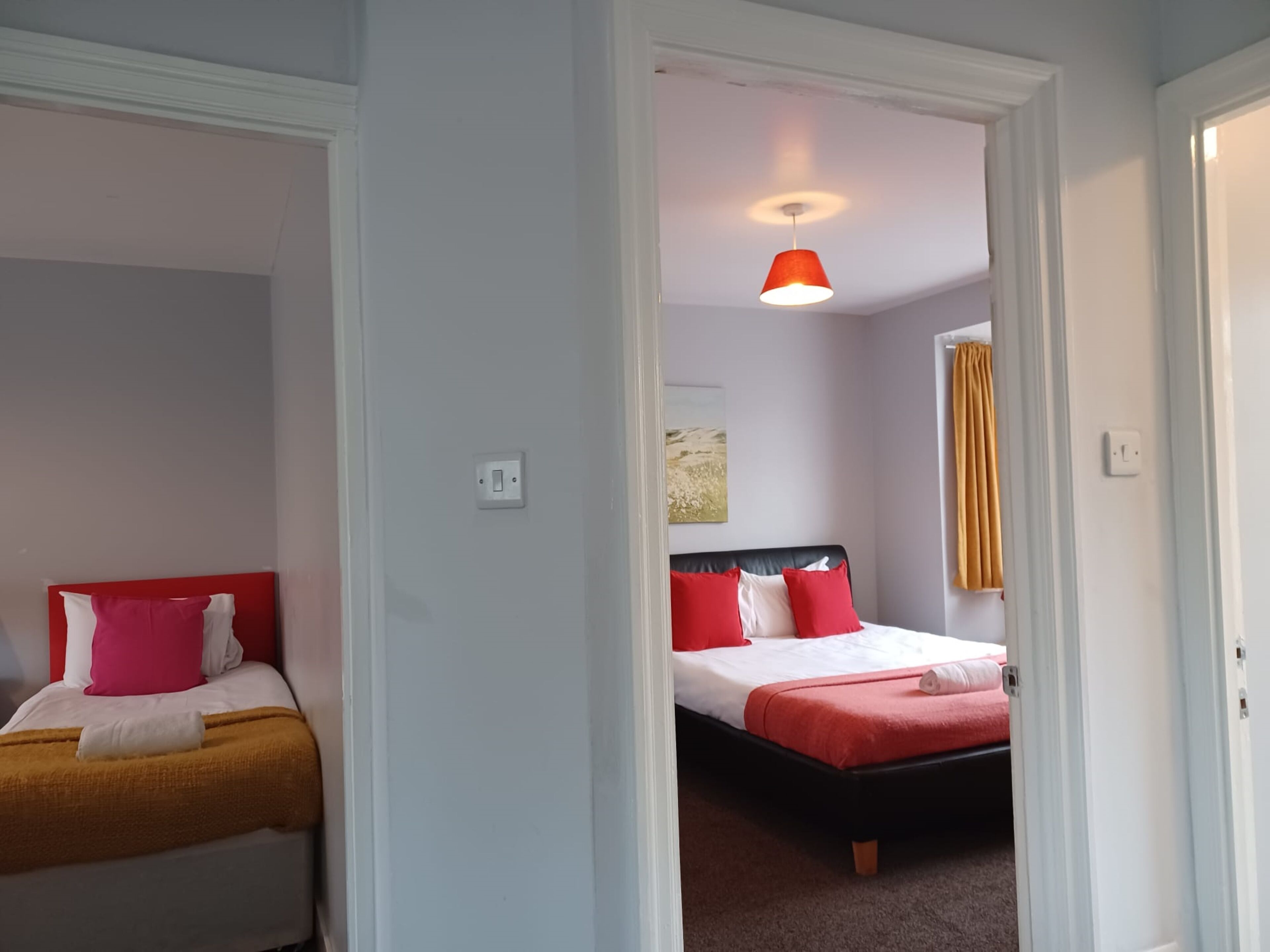 Quarto de hotel com duas camas, cada uma com roupa de cama vermelha e branca, uma luminária de teto vermelha e um quadro na parede.