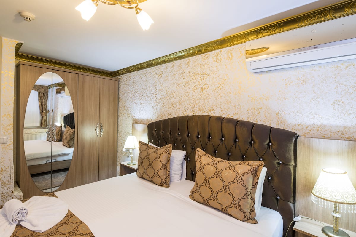 Quarto de hotel com uma cama grande, um espelho, um guarda-roupa e uma mesa de cabeceira com abajur.