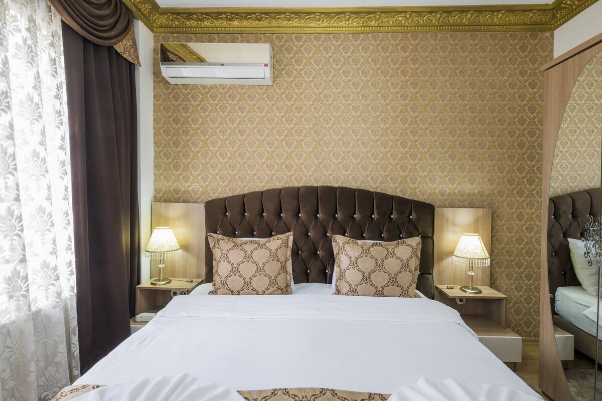 Quarto de hotel com uma cama grande, duas mesas de cabeceira com abajures, ar-condicionado fixado na parede e papel de parede estampado.