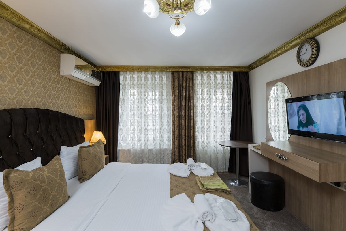 Quarto de hotel com uma cama grande, televisão, escrivaninha e cadeira.