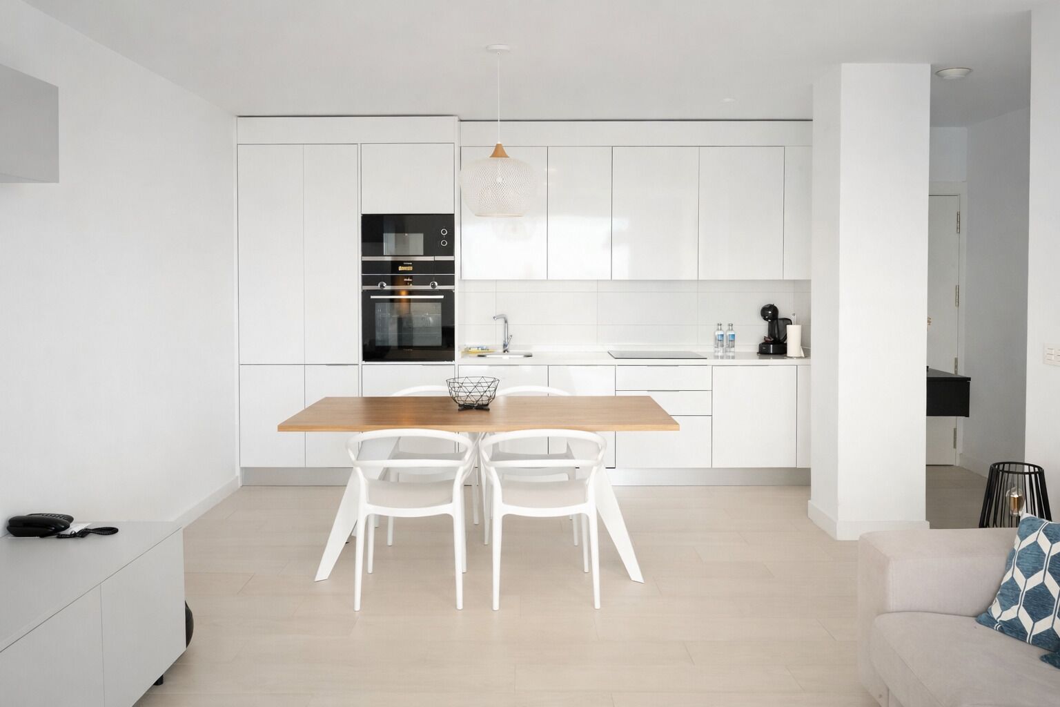 Uma cozinha moderna com armários brancos, uma mesa de jantar de madeira e duas cadeiras brancas.