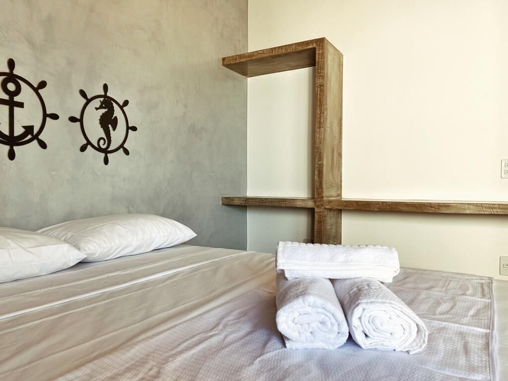 Quarto de hotel com uma cama, almofadas, cabeceira de madeira e espelho fixado na parede.