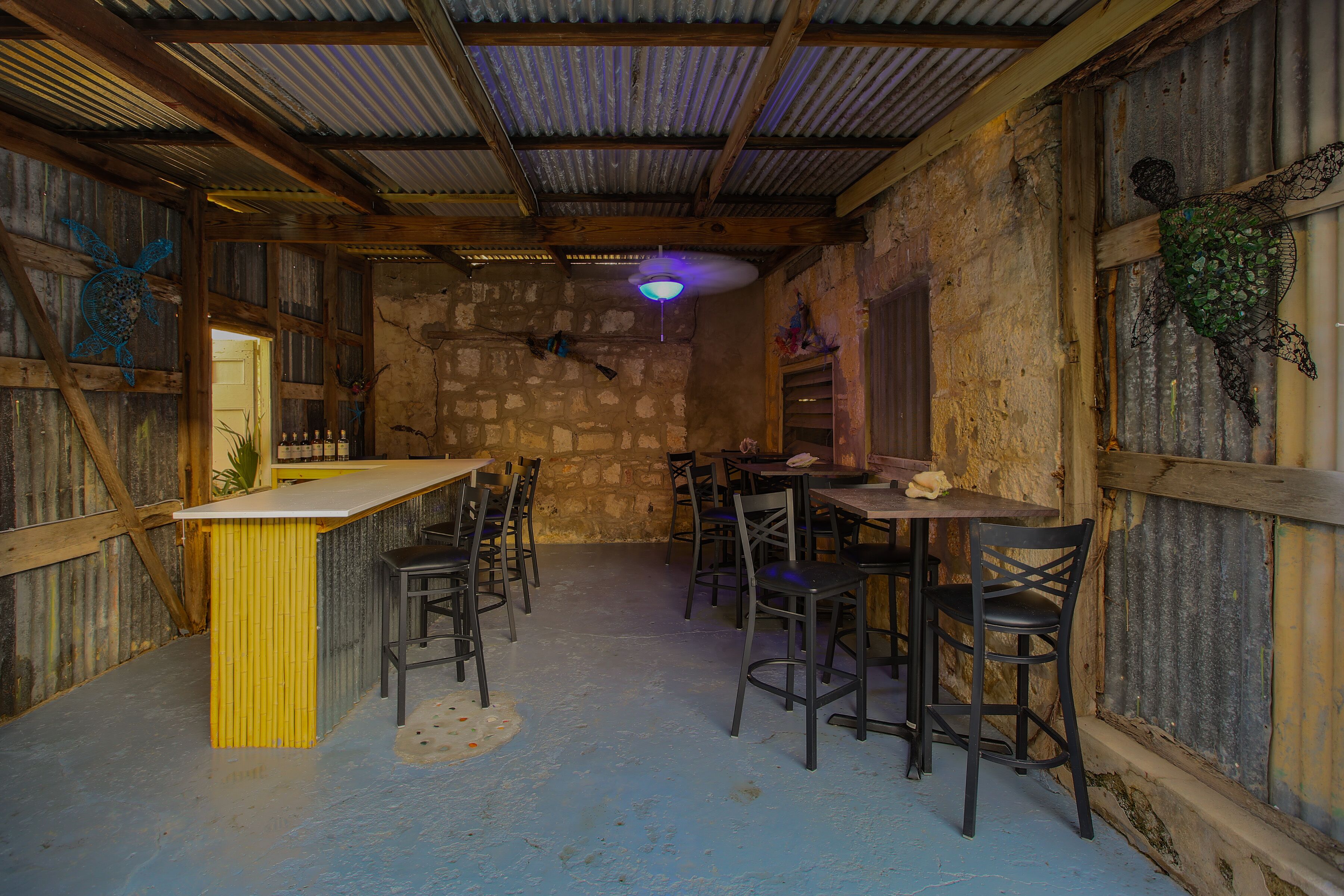 Um espaço de bar rústico com mobiliário de madeira, parede de pedra e teto de metal corrugado.