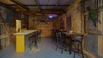 Um espaço de bar rústico com mobiliário de madeira, parede de pedra e teto de metal corrugado.
