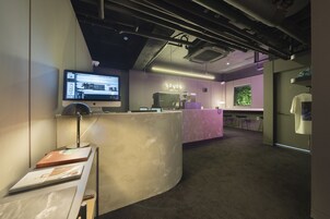 Uma área de recepção com um balcão curvo, uma máquina de café, uma televisão e uma placa com a inscrição "goyos hotel".