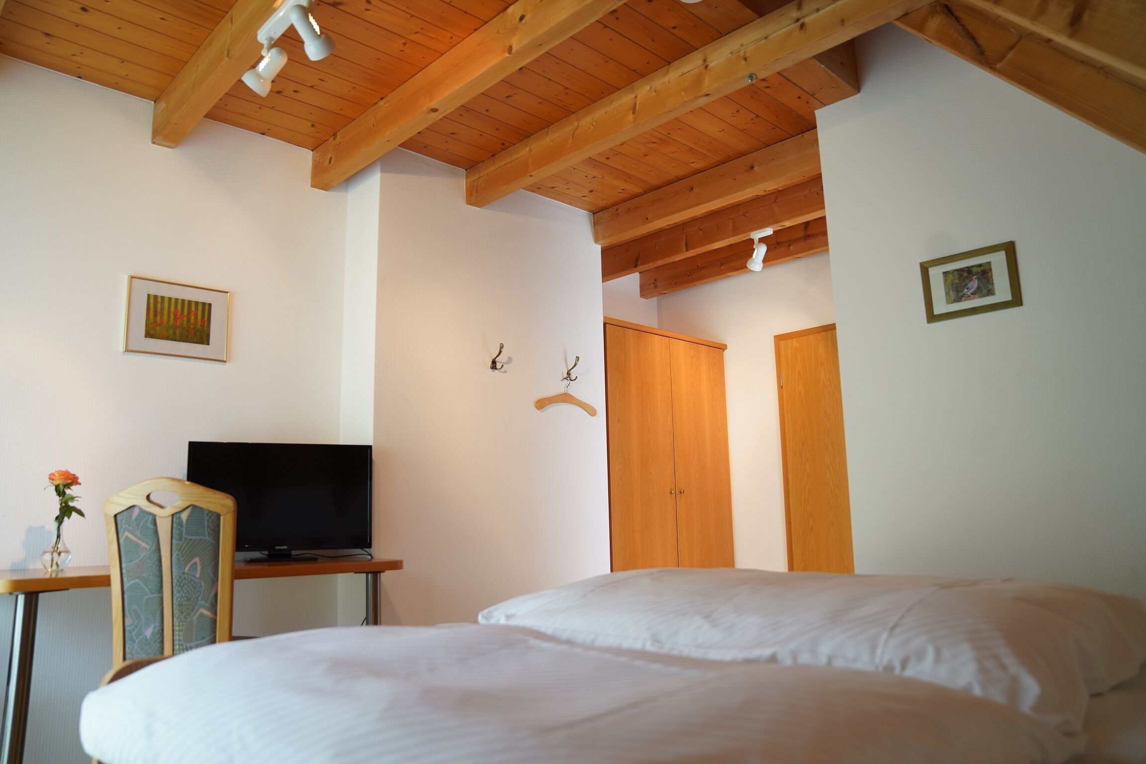 Quarto com teto de madeira, uma cama, uma televisão sobre uma escrivaninha e um guarda-roupa.