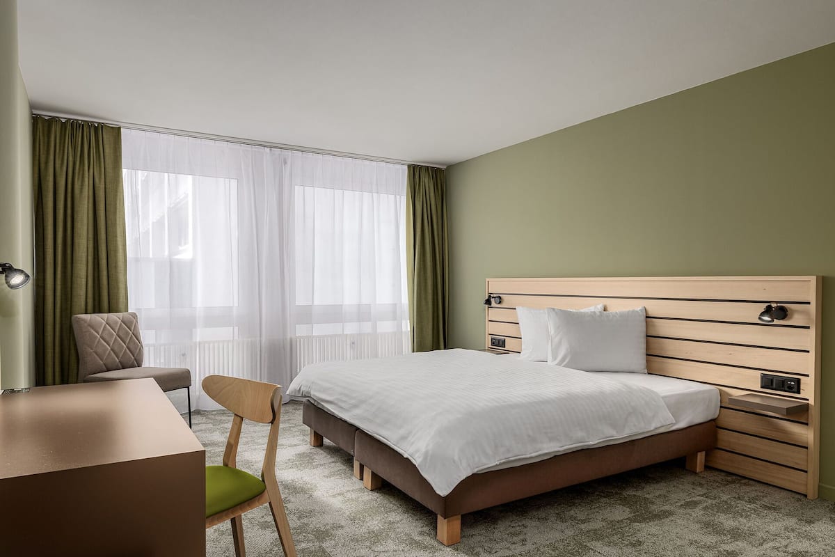 Quarto de hotel com cama, mesas de cabeceira, escrivaninha e uma cadeira.