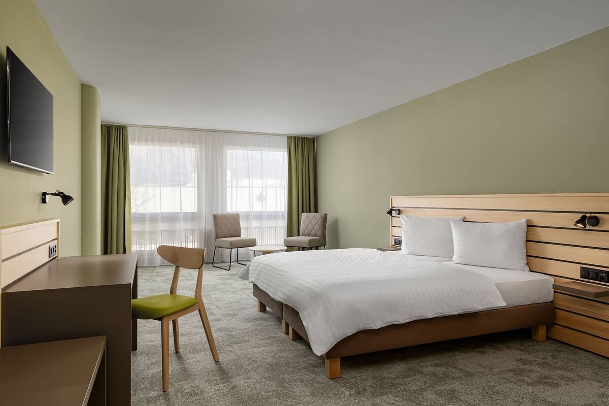 Quarto de hotel com cama, secretária, cadeira e televisão.