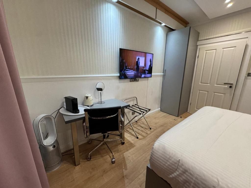 Quarto de hotel com cama, escrivaninha e cadeira, televisão fixada na parede e porta.