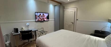 Quarto de hotel com uma cama, uma mesa com computador, uma cadeira, televisão fixada na parede e uma porta.