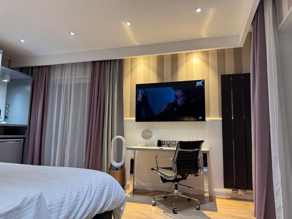 Quarto de hotel com cama, escrivaninha, computador, televisão e guarda-roupa.