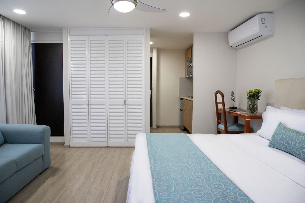 Quarto de hotel com cama, escrivaninha, cadeira, guarda-roupa e ar condicionado.