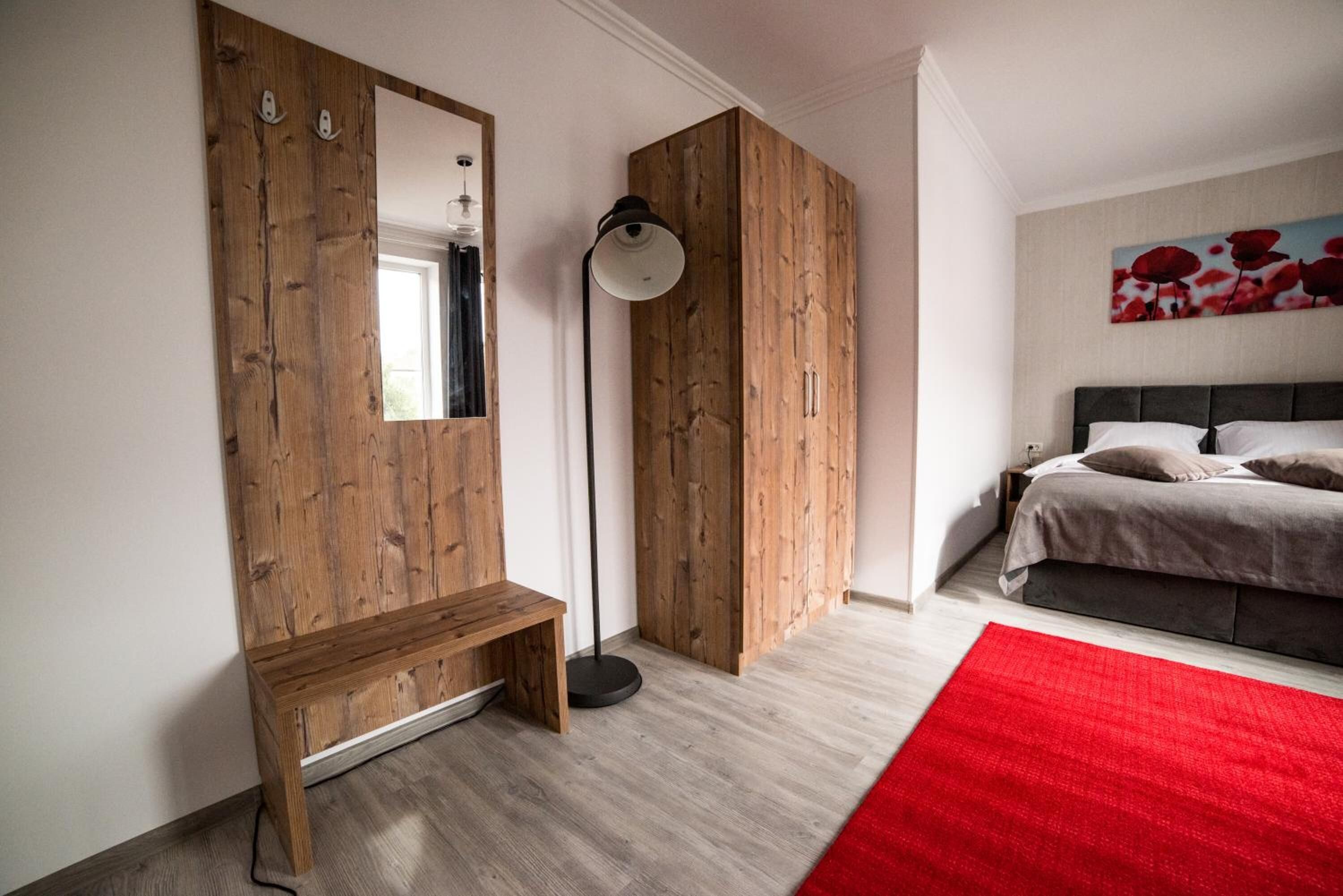 Quarto com guarda-roupa de madeira, mesa de cabeceira, abajur e cama com tapete vermelho.