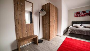 Quarto com guarda-roupa de madeira, mesa de cabeceira, abajur e cama com tapete vermelho.