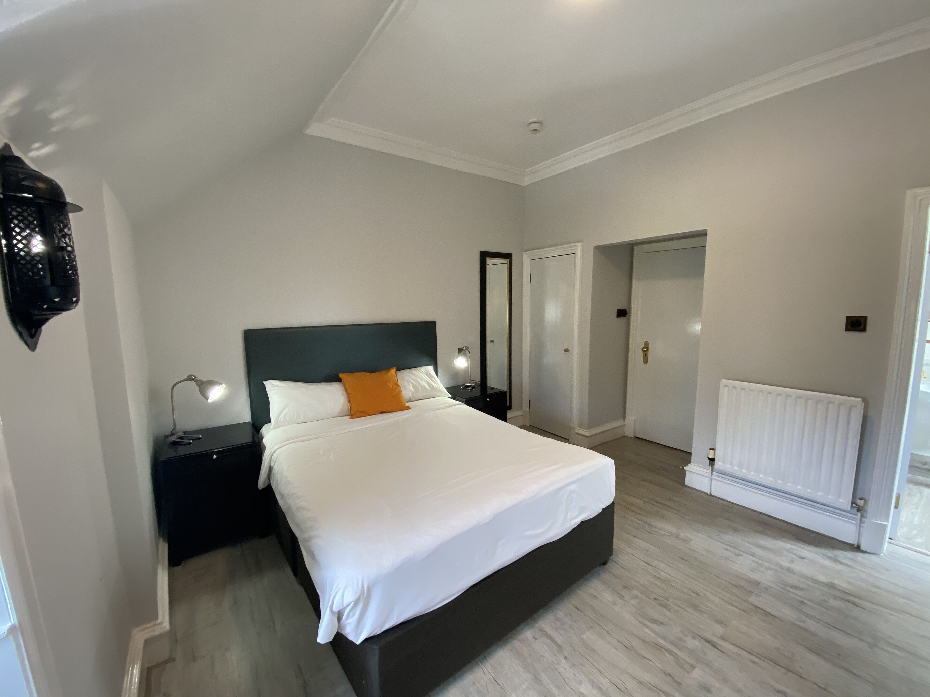 Quarto com cama, mesas de cabeceira, espelho e radiador.