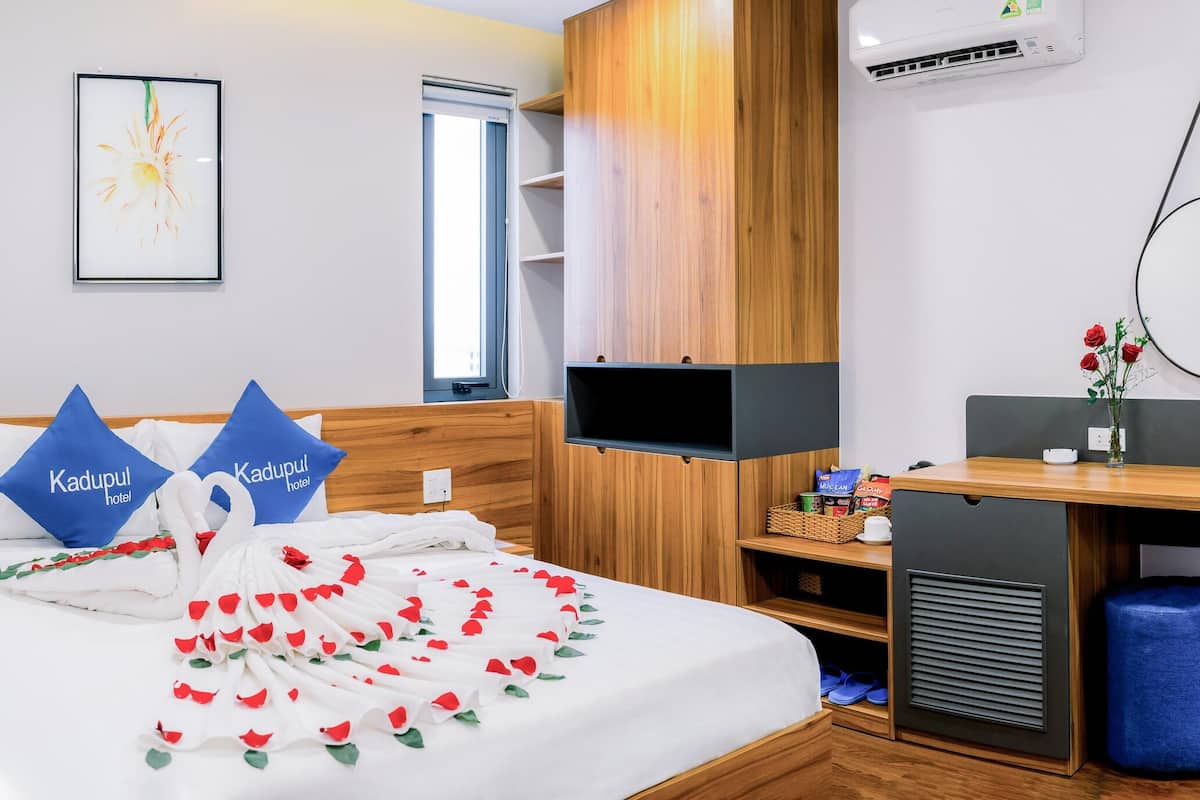 Quarto de hotel com cama, escrivaninha, televisão e espelho.
