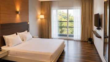 Quarto de hotel moderno com uma cama grande, ventilador de teto, televisão e vista para o verde pela janela.