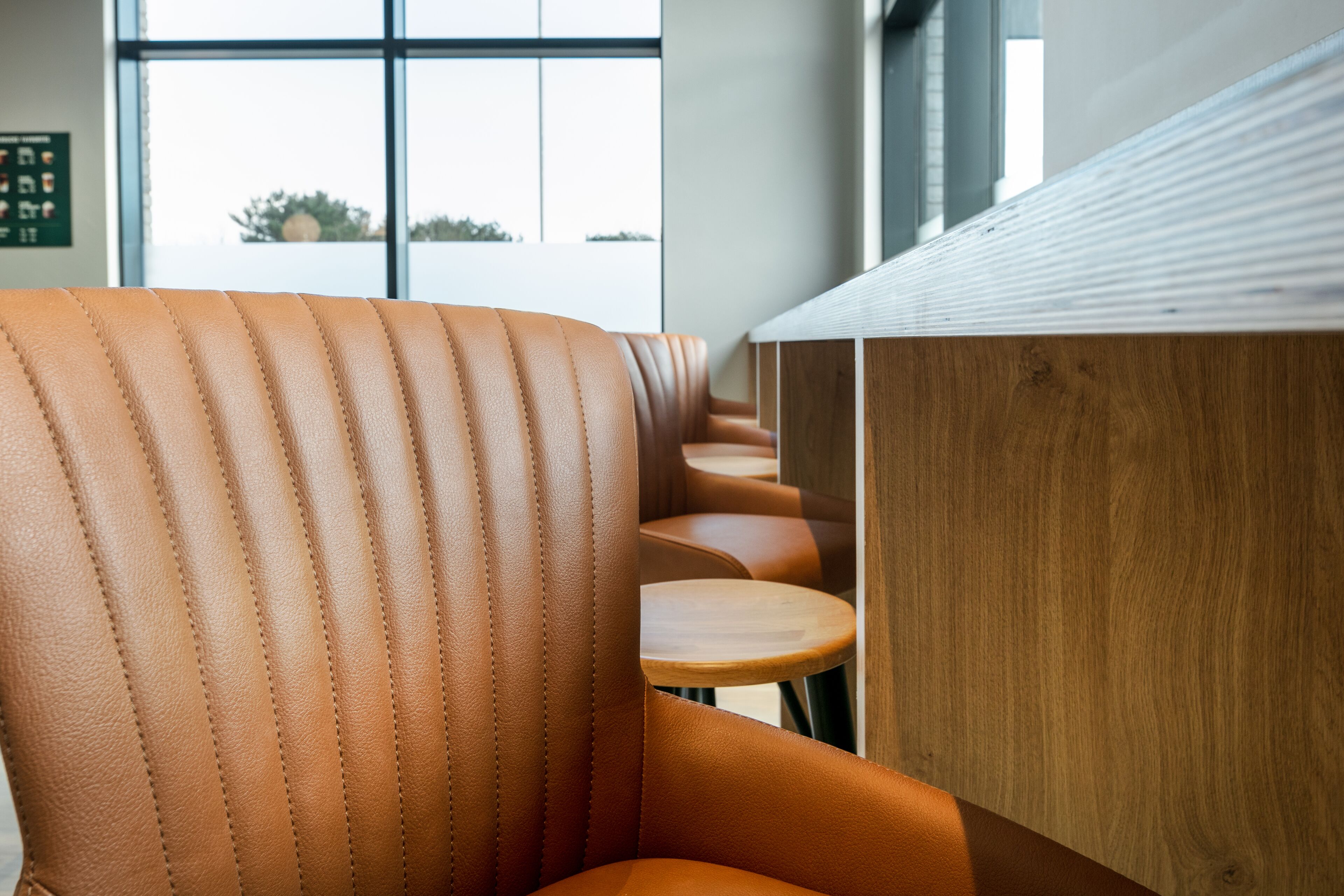 Interior moderno com poltronas de couro e mesas de madeira, janelas amplas e design limpo e minimalista.