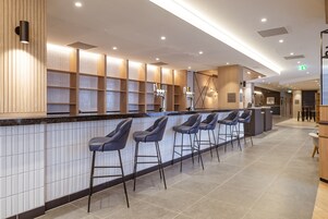 Uma área de bar moderna com um balcão comprido, vários banquinhos e um revestimento de azulejos.