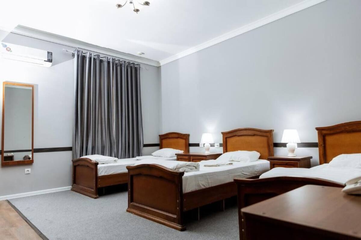 Quarto de hotel com quatro camas de solteiro, um espelho grande, um ventilador de teto e uma janela com cortinas.
