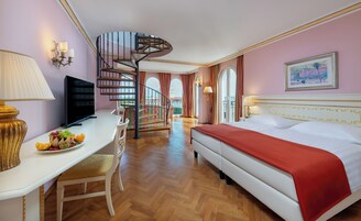 Quarto de hotel com cama, escrivaninha, cadeira e escada espiral que dá para uma varanda externa.