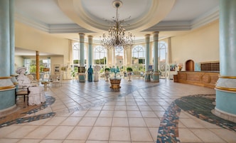 Um hall amplo com um lustre imponente, colunas e piso revestido com borda em mosaico.