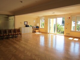 Um quarto espaçoso com piso em padrão herringbone, uma cozinha compacta, um espaço de refeições com cadeiras e grandes janelas com vista para o verde.