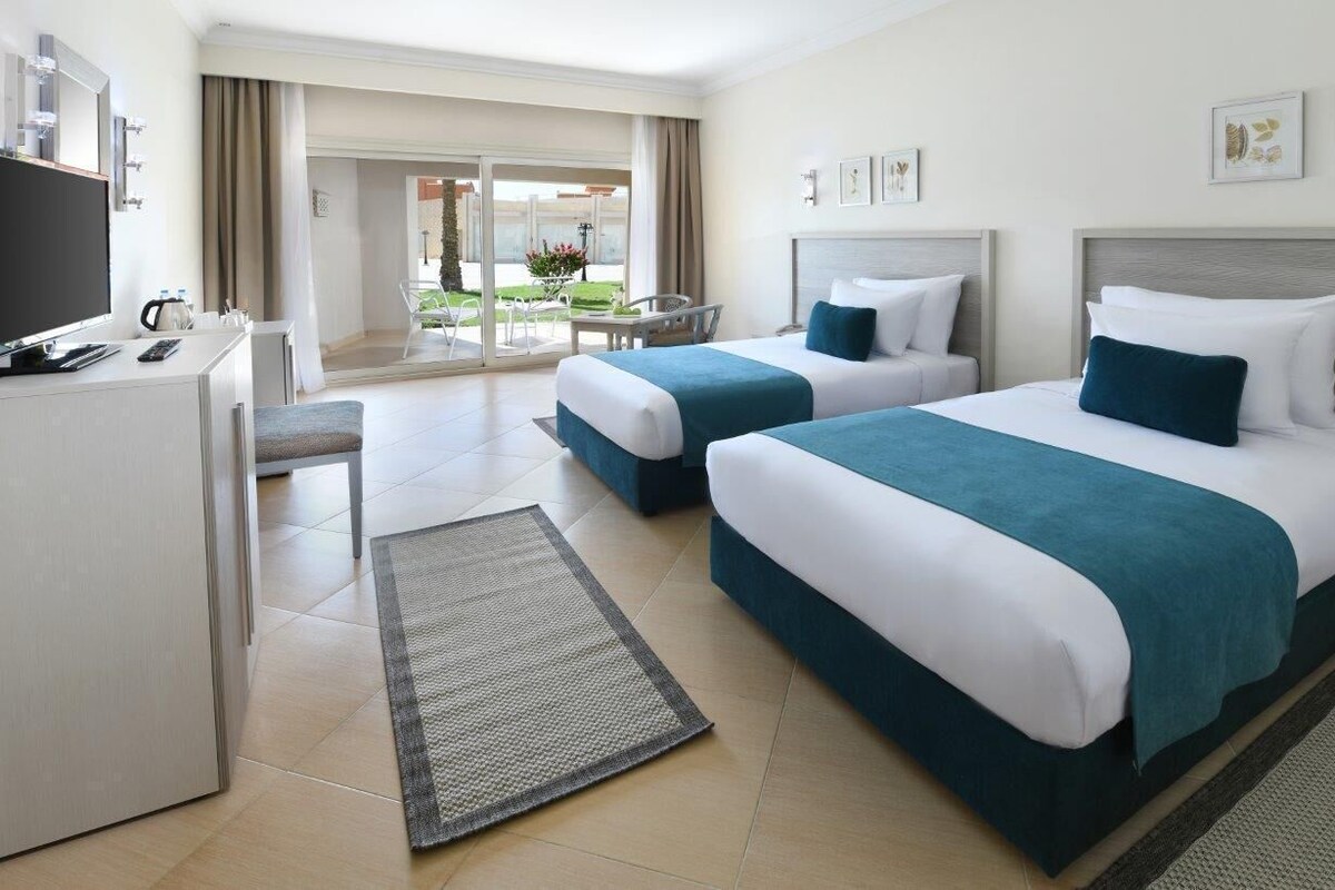 Quarto de hotel com duas camas, uma mesa de trabalho com televisão e uma varanda com vista.